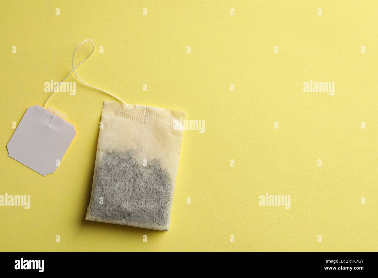 Paper tea bag with tag on yellow background, top view. Space for text ...