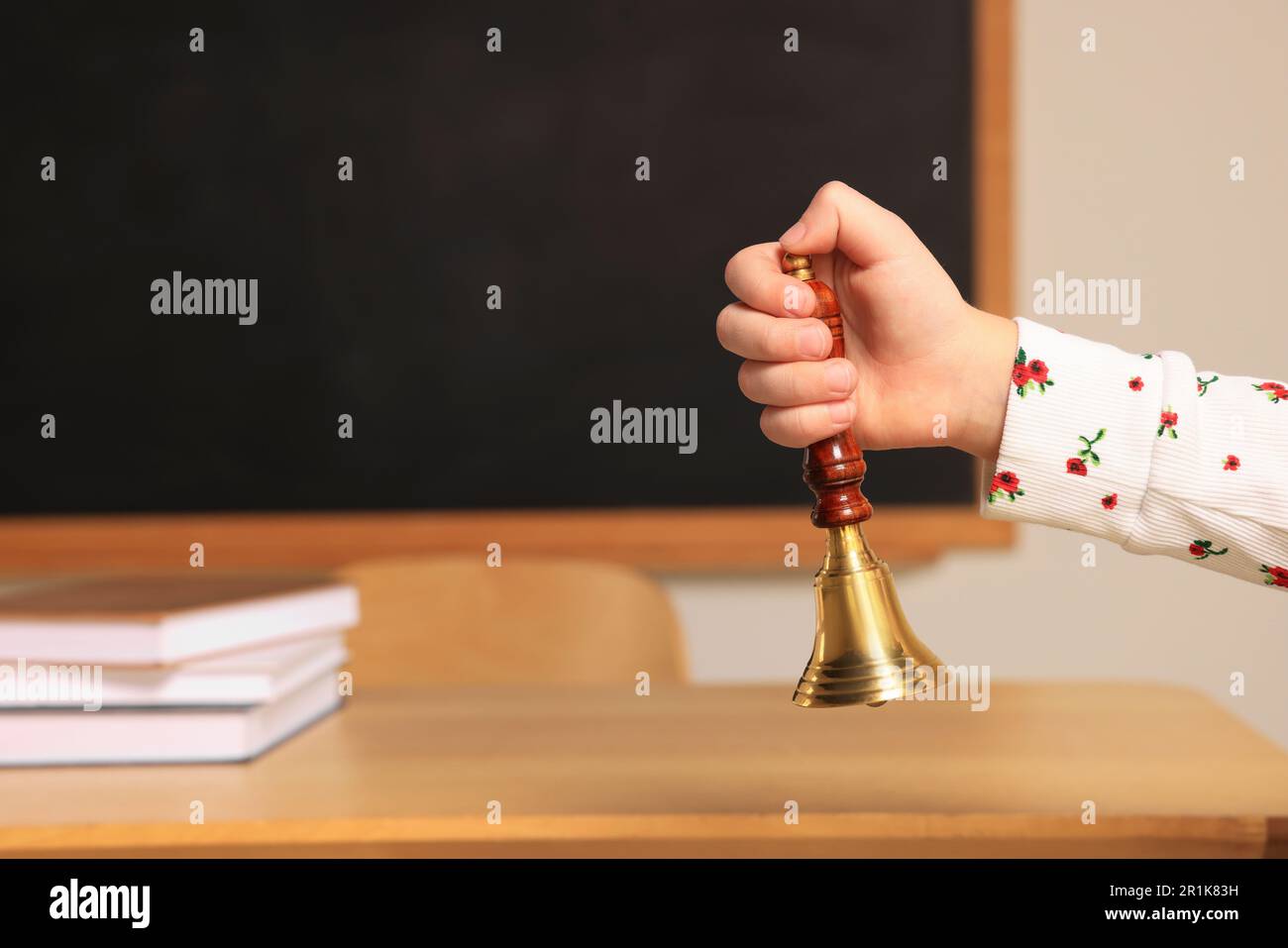 Pupil with school bell near desk and chalkboard in classroom, closeup ...