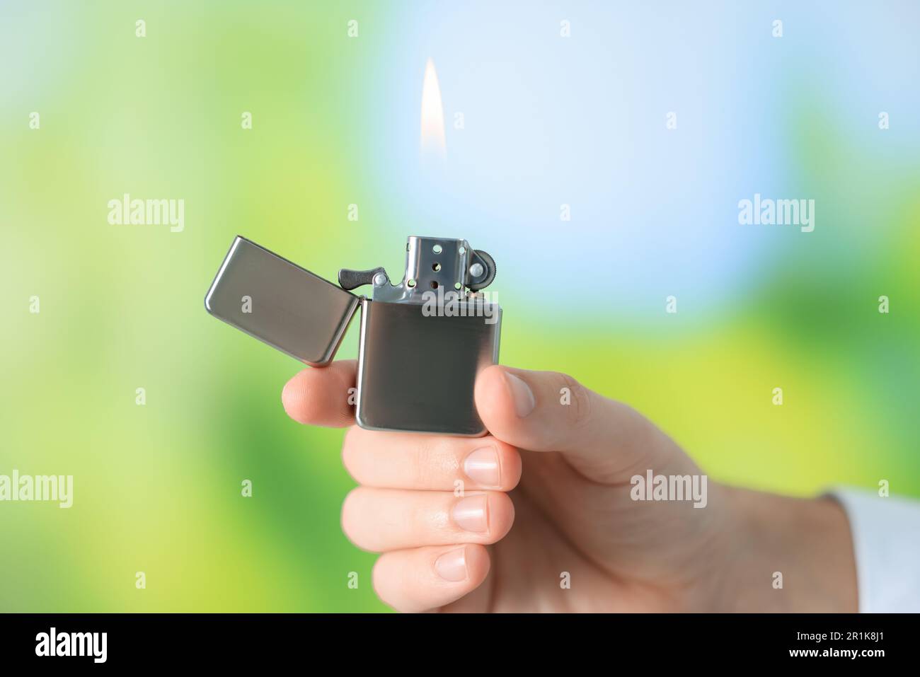 Man holding lighter with burning flame against blurred green background ...