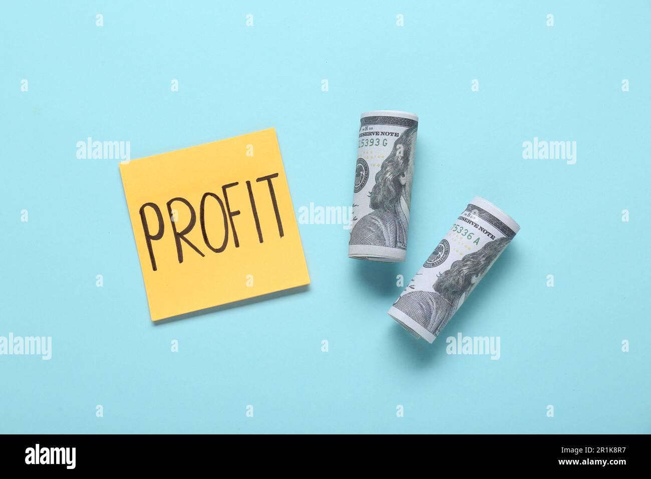 Sticky note with word Profit and rolled banknotes on turquoise ...