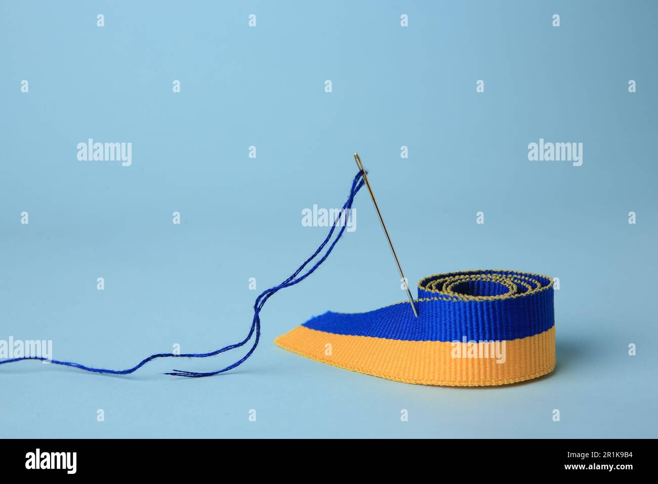 Sewing needle with thread and color ribbon on light blue background ...