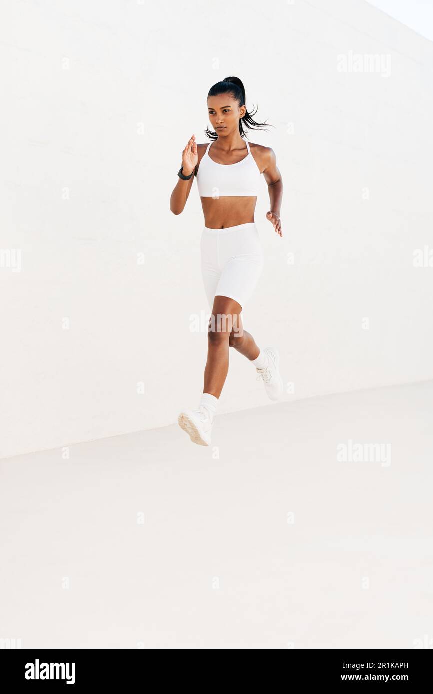 Full length of young slim woman sprinting outdoors at white wall. Fit woman running fast Stock ...