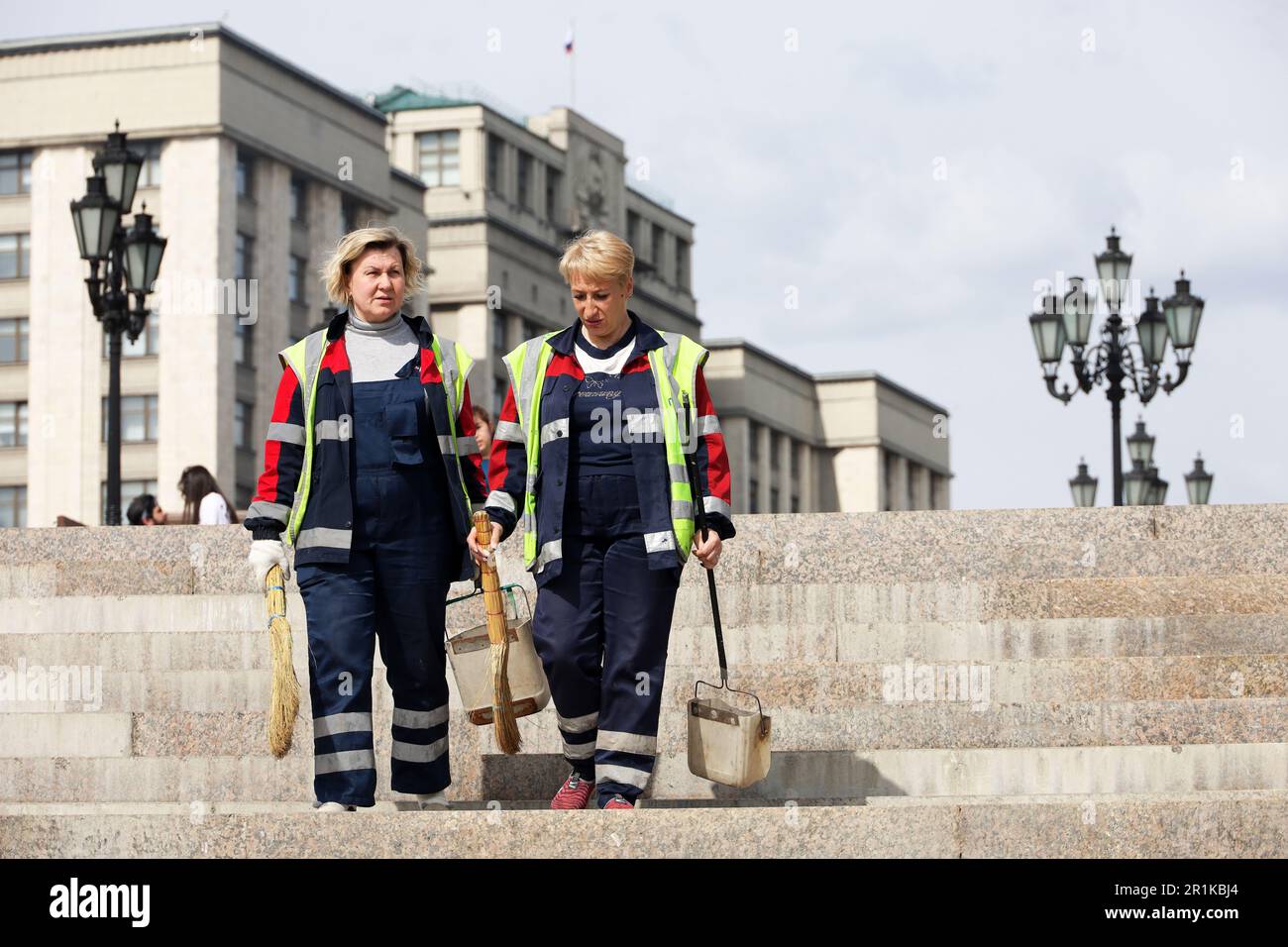 Two female janitors go down the stairs on State Duma background ...