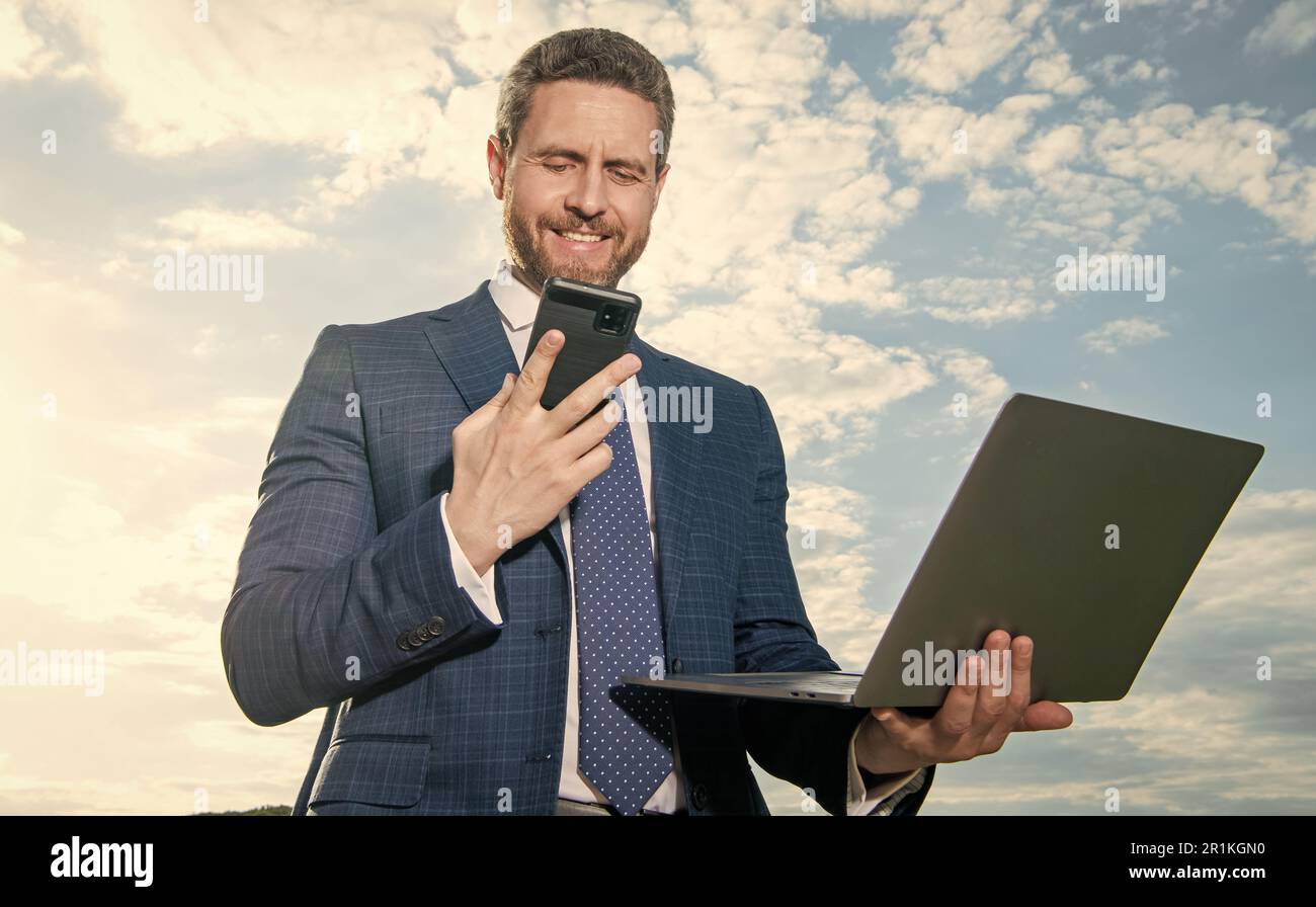 smiling freelancer man with laptop and phone on sky. freelancer man ...