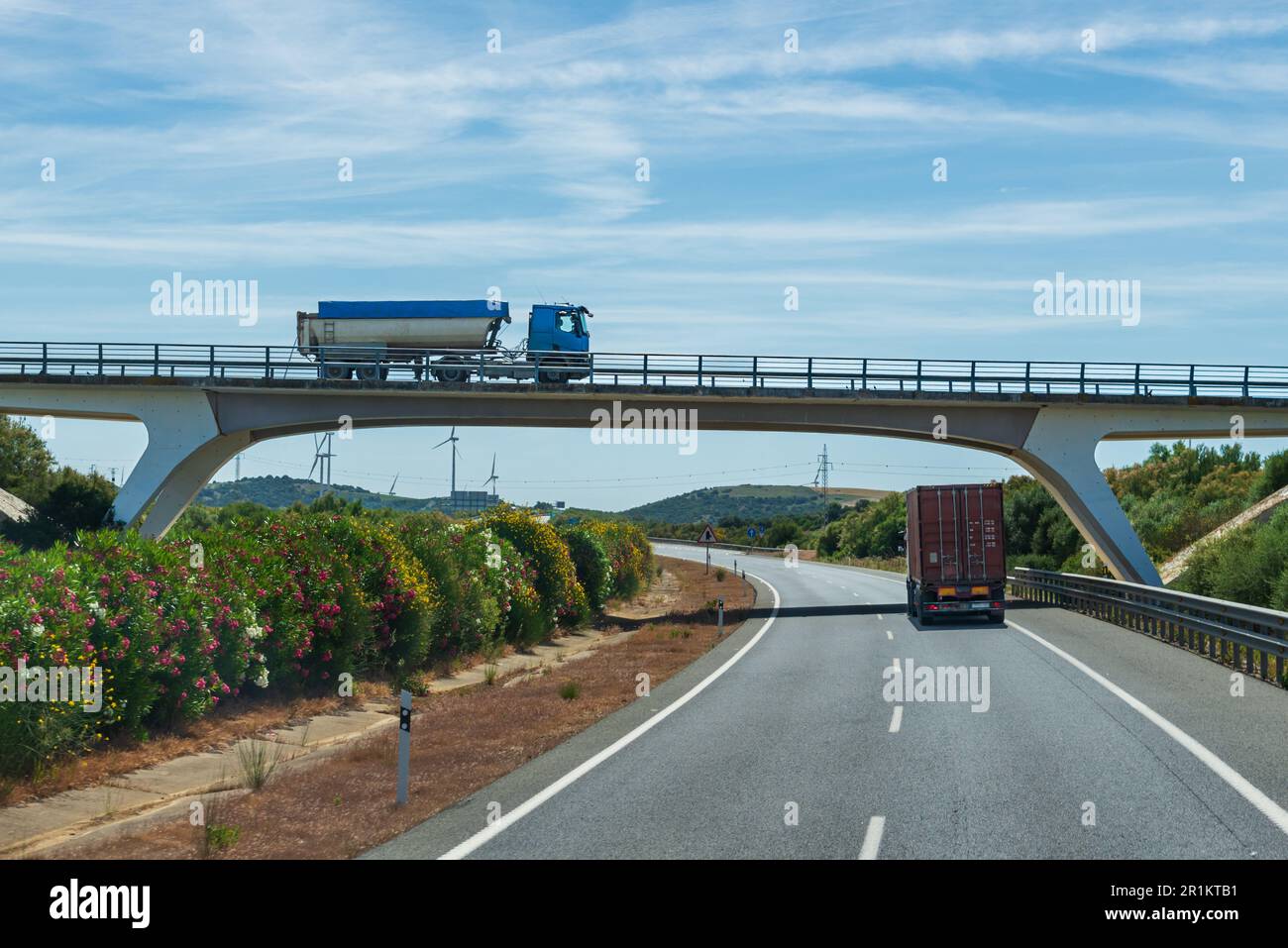 Container truck driving on a highway while another truck passes over a ...