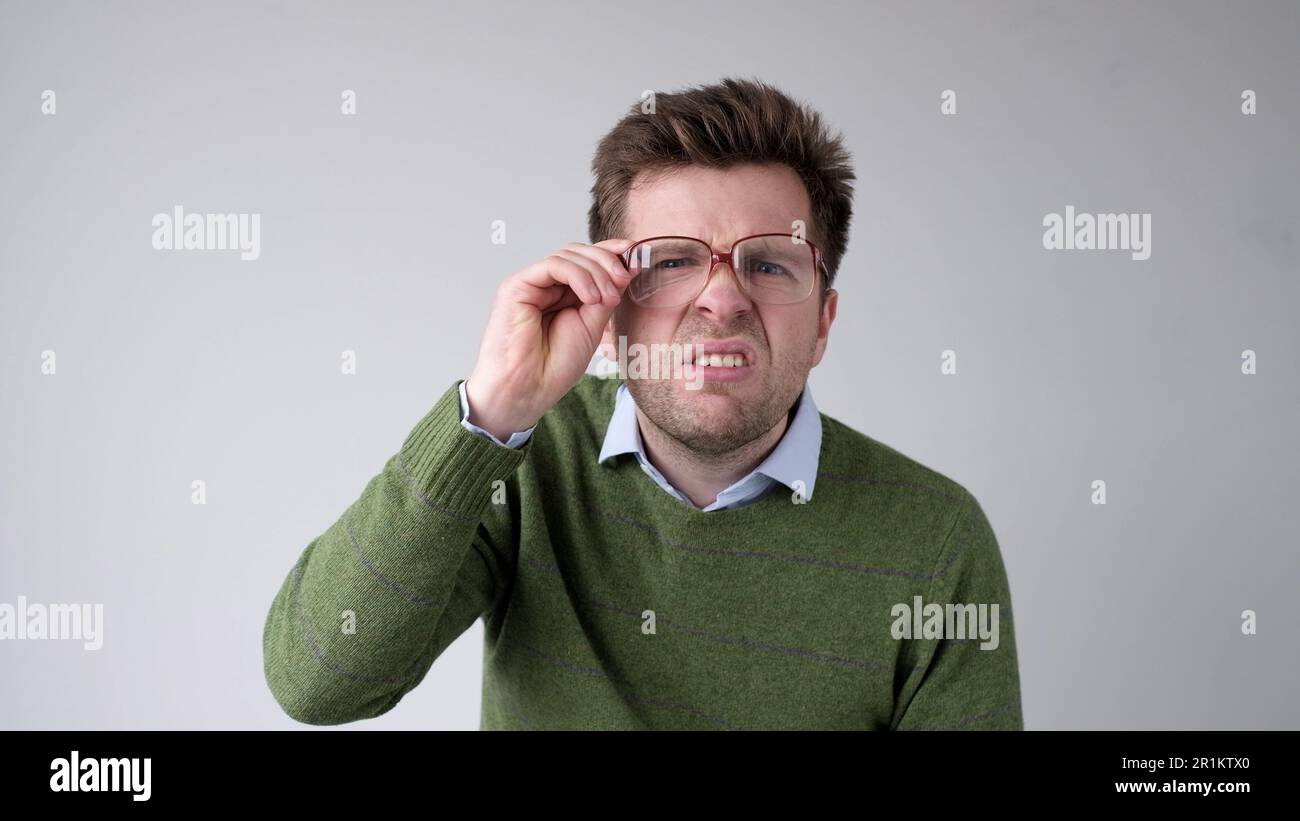 European young man with poor vision peers through his glasses, trying ...