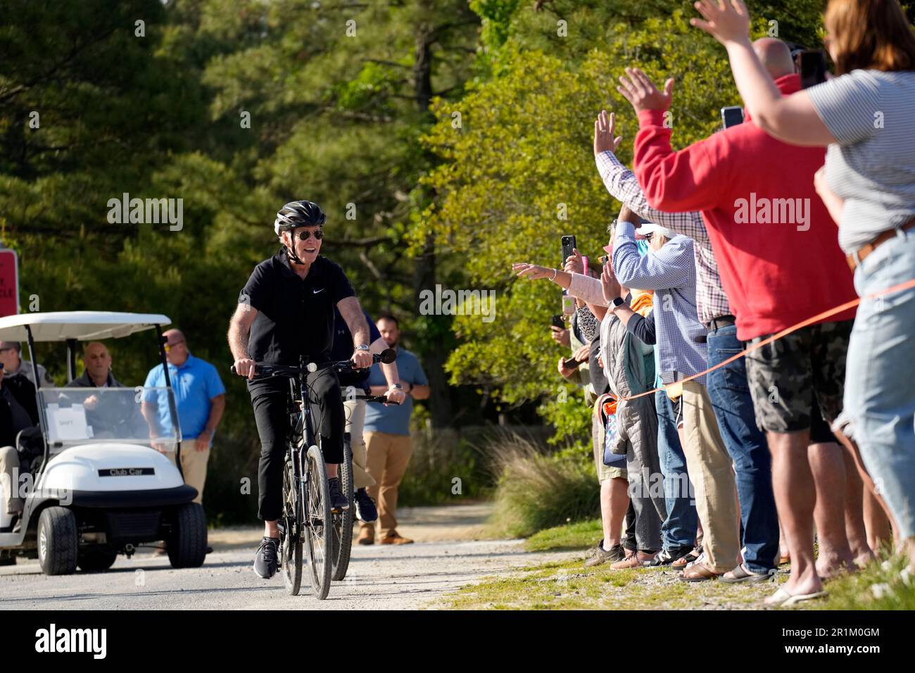 People wave to President Joe Biden as he goes on a bike ride in Gordons ...