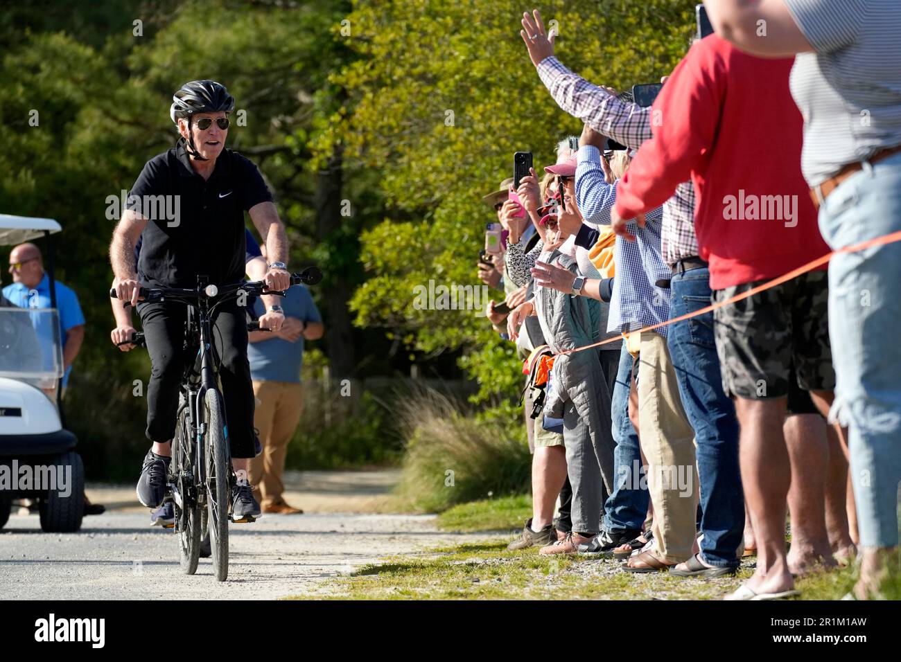 People wave to President Joe Biden as he goes on a bike ride in Gordons ...
