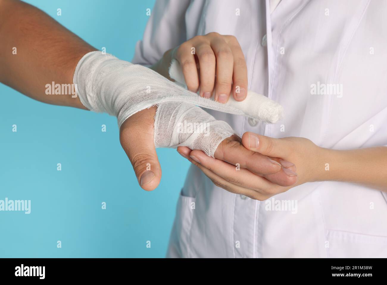 Doctor applying bandage onto patient's hand on light blue background ...