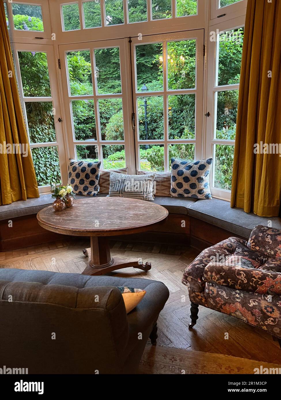 Wooden table near bay window seat with cushions in cozy room. Interior ...