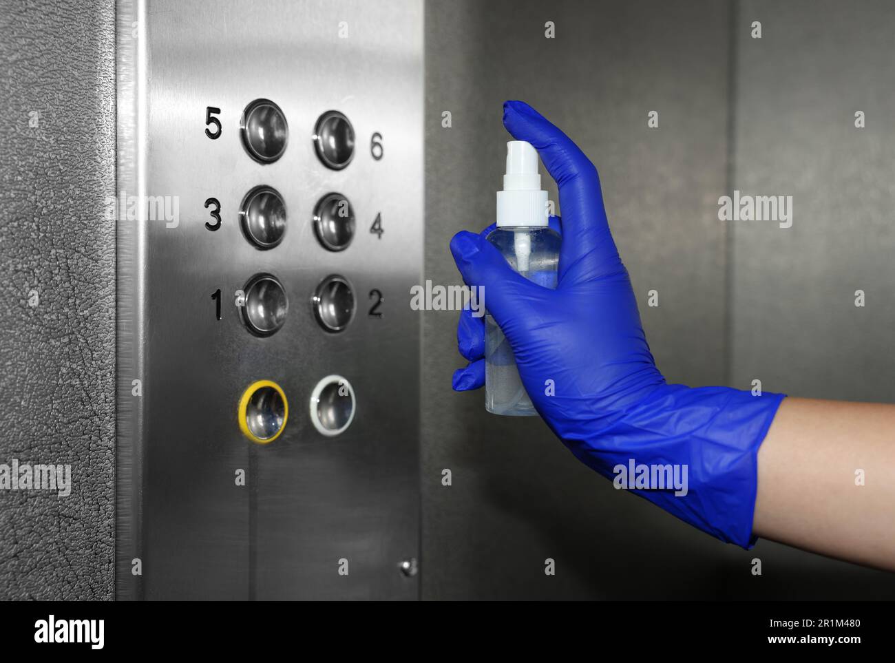 Woman cleaning buttons panel in elevator with detergent spray, closeup ...