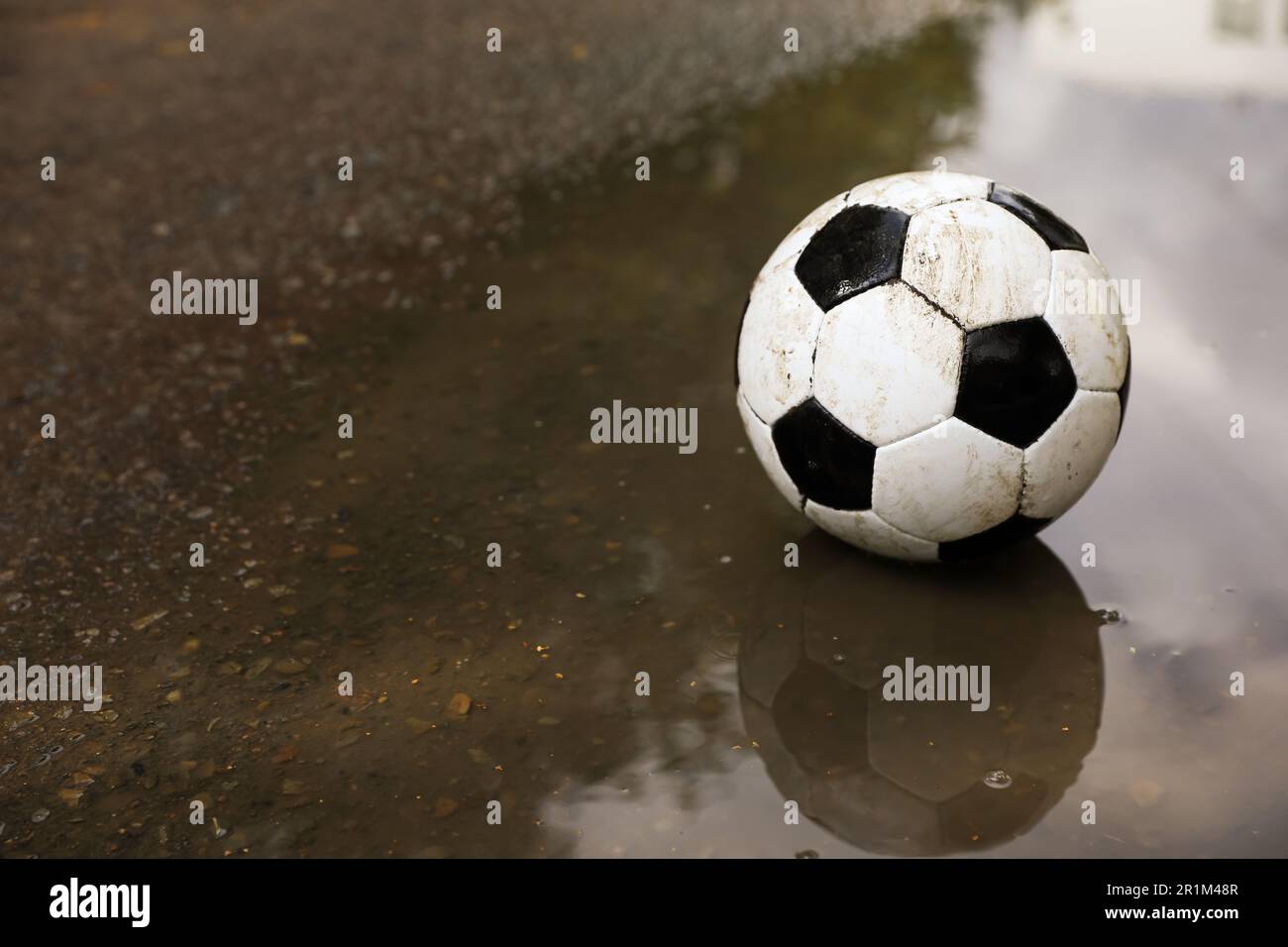 Dirty soccer ball near puddle outdoors, space for text Stock Photo - Alamy
