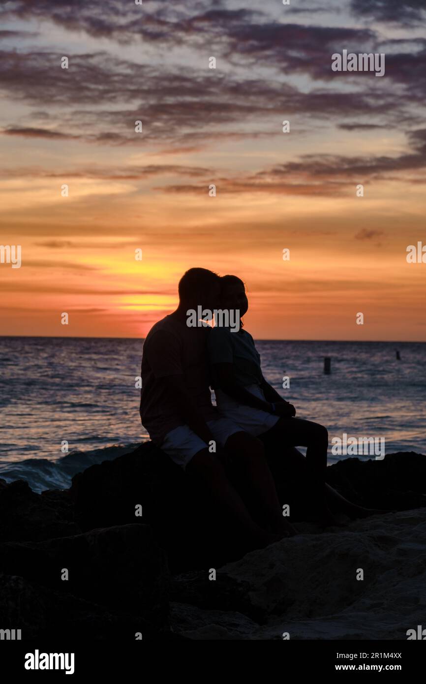 A couple of men and women are on the beach watching the sunset during ...