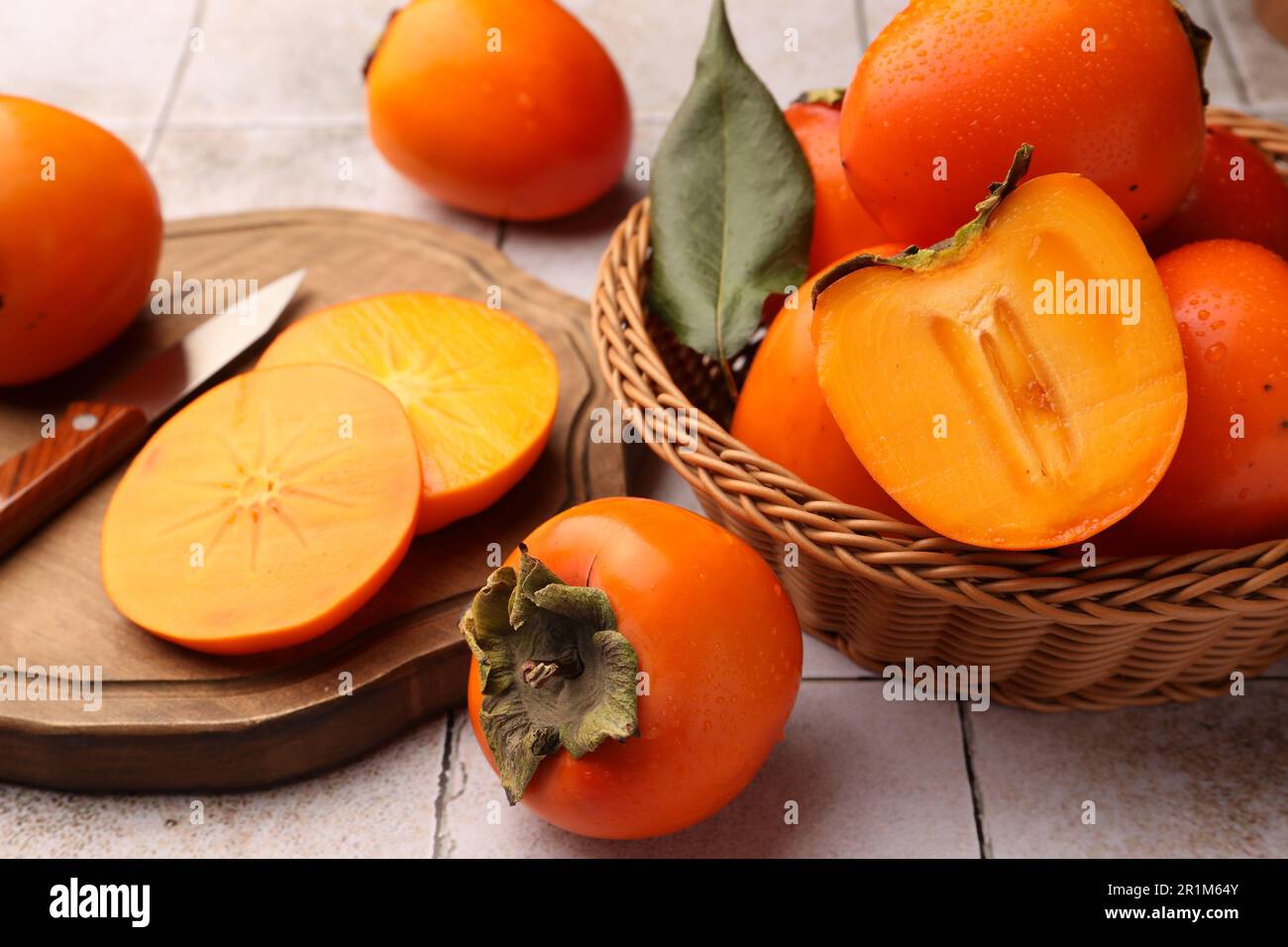Delicious ripe juicy persimmons in wicker basket on tiled surface Stock ...