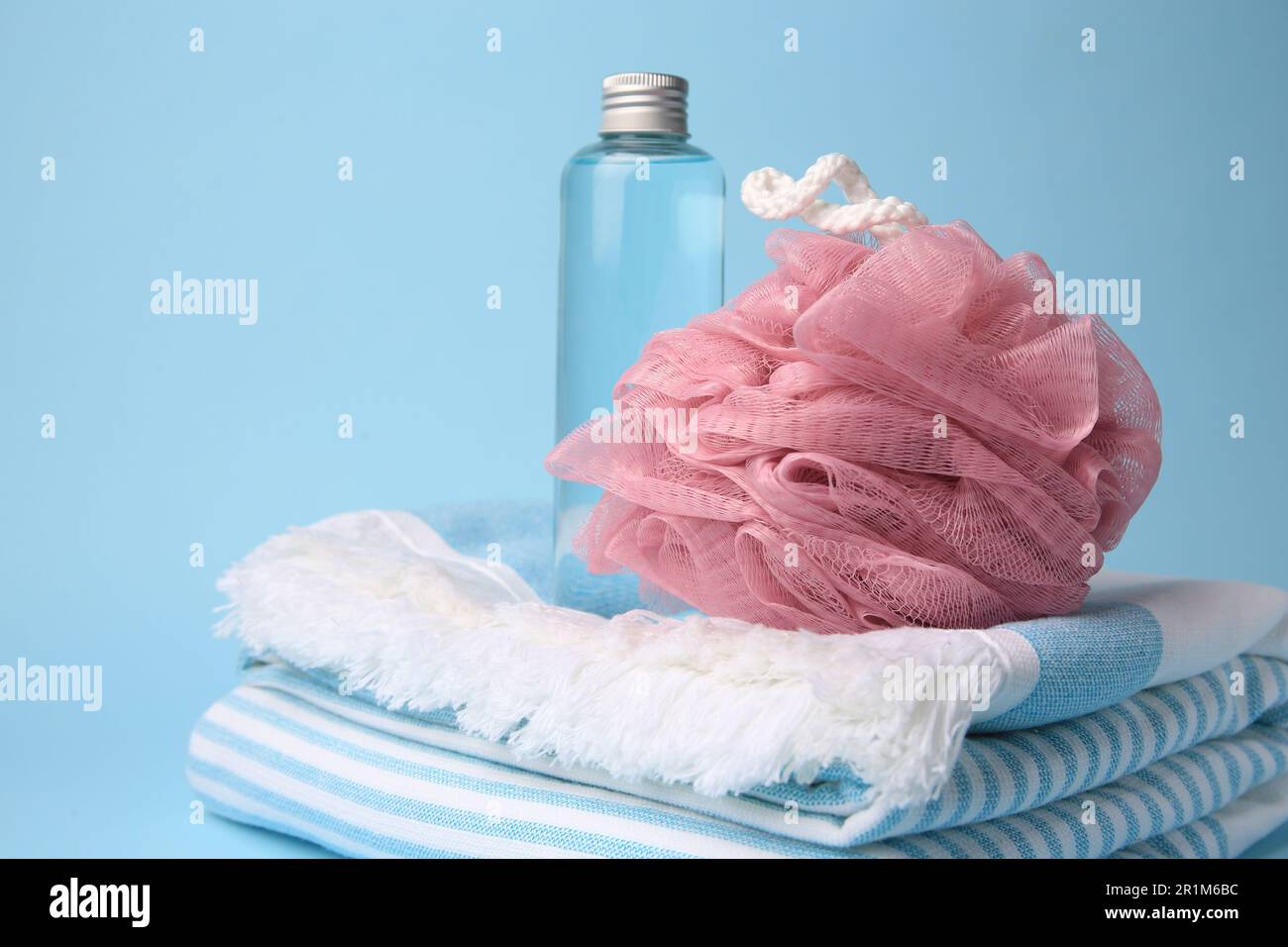 Pink shower puff, bottle of cosmetic product and towel on light blue ...