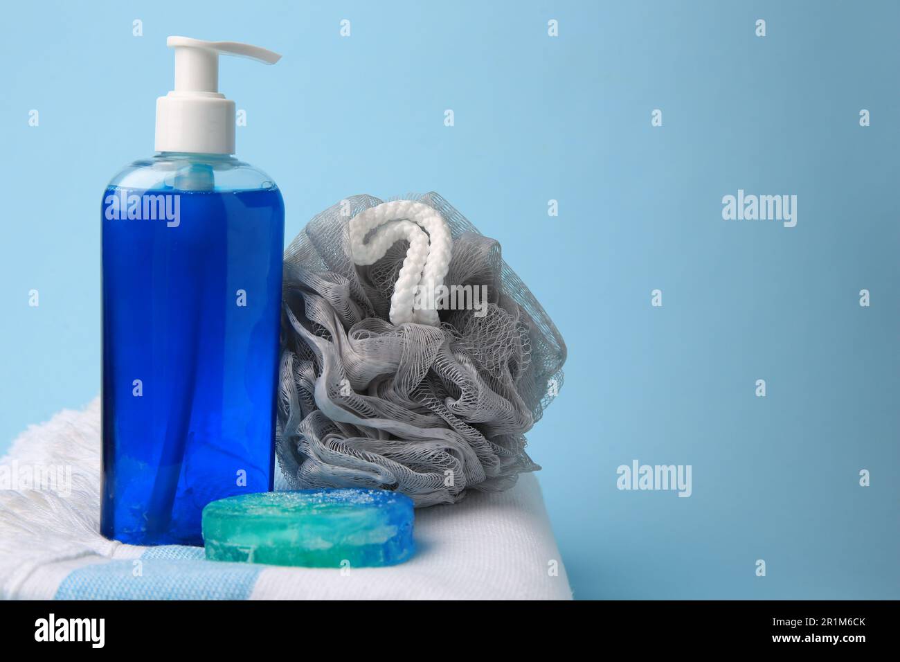 Grey shower puff, cosmetic products and towel on light blue background ...