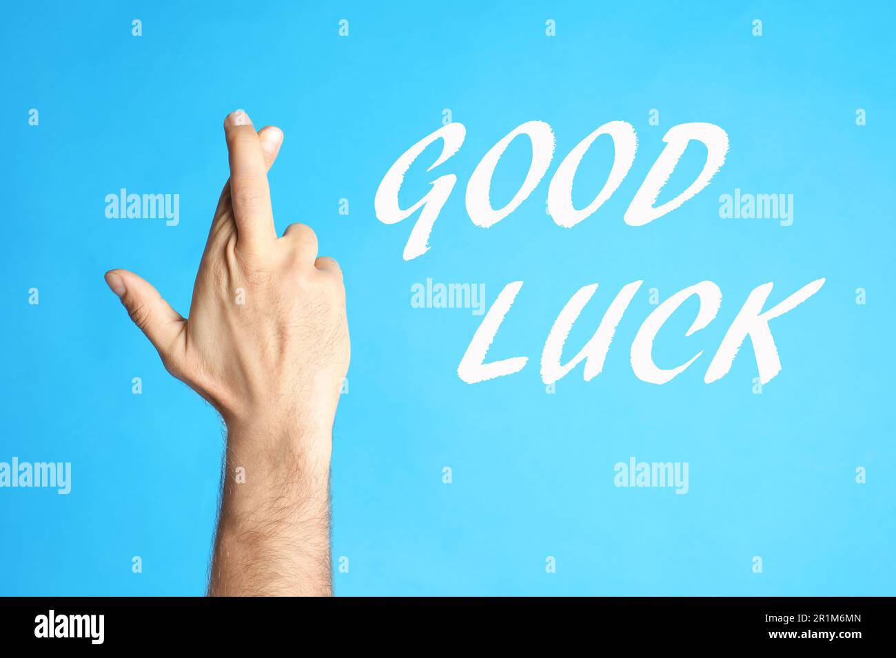 Man with crossed fingers on light blue background, closeup. Good luck ...