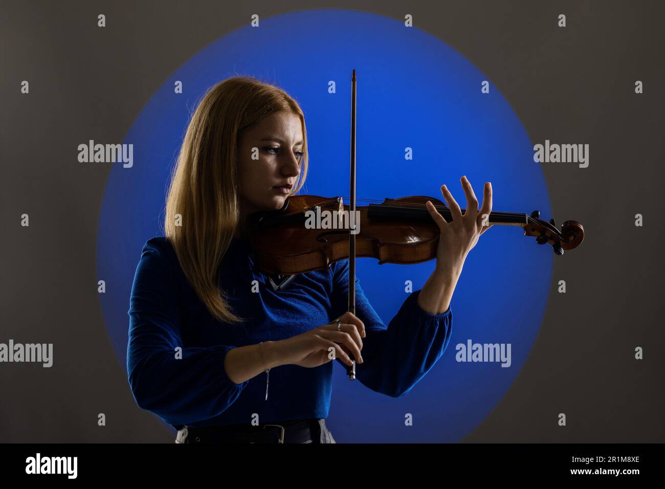 Beautiful blond girl playing violin. Female violinist against dark blue ...