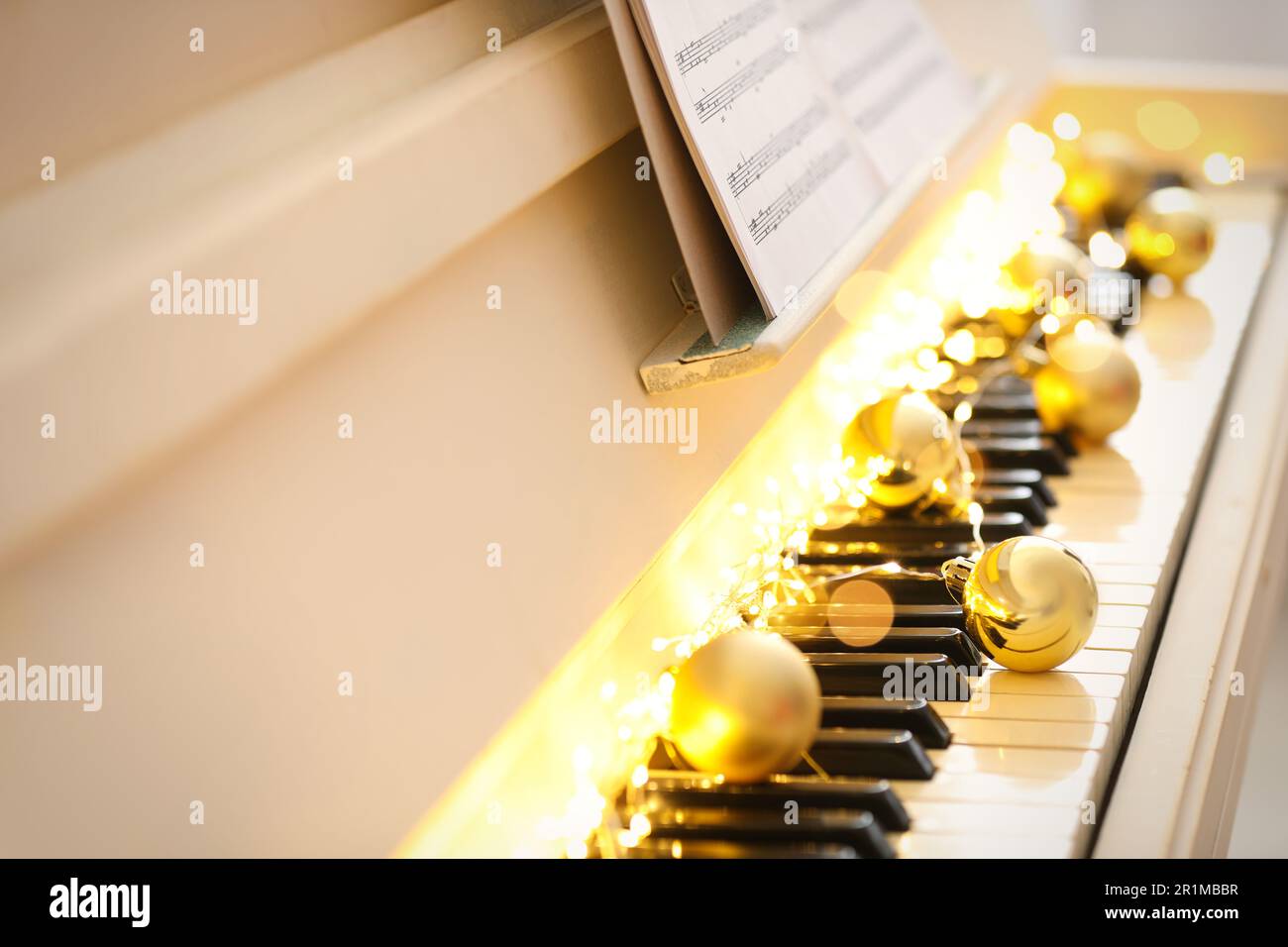 Golden baubles and fairy lights on piano keys, closeup. Christmas music ...