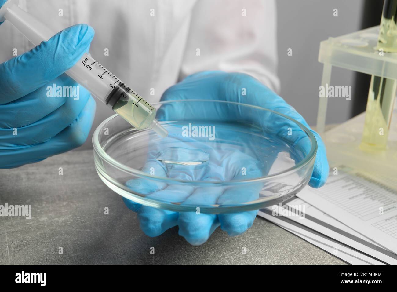 Doctor dripping urine from syringe into petri dish at grey table ...