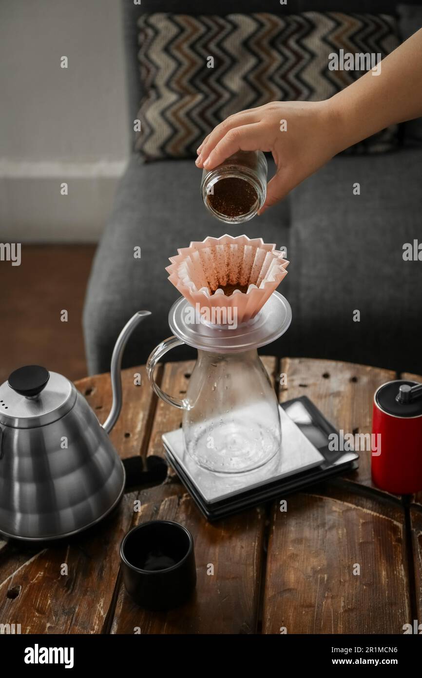 Barista putting coffee into jug with wave dripper at wooden table in ...