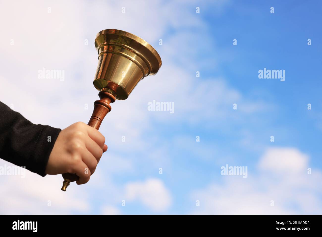 Pupil with school bell against cloudy sky, closeup. Space for text ...