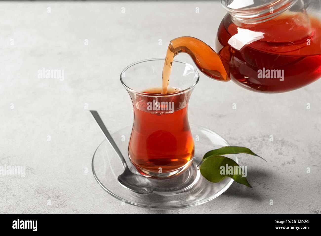 Pouring traditional Turkish tea from pot into glass on light grey table ...