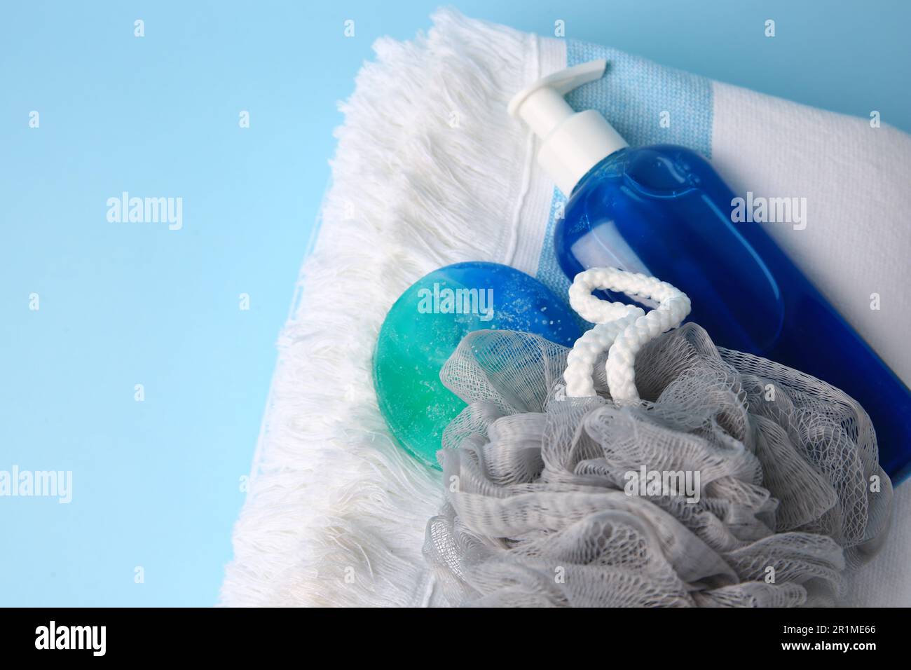 Grey shower puff, cosmetic products and towel on light blue background ...