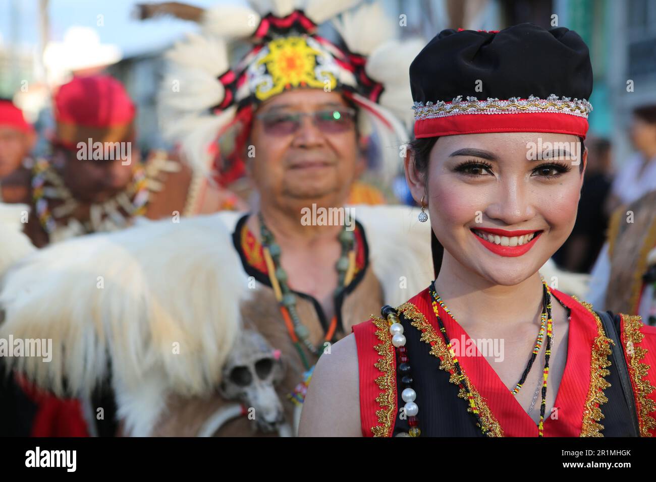 A similing Bidayuh lass walking in front of an Orang Ulu Chief in ...