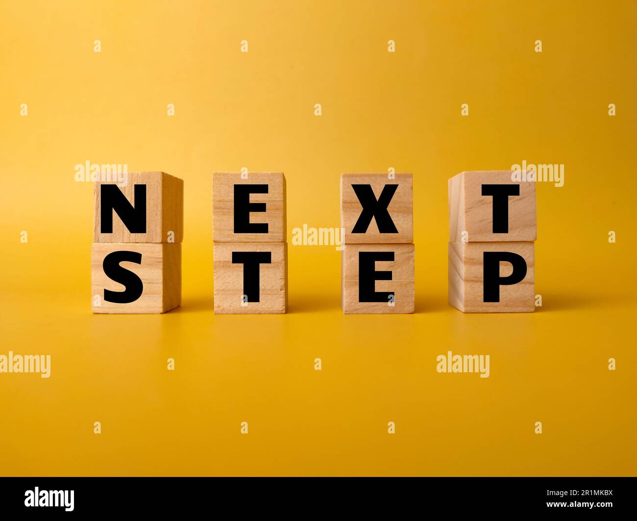 Wooden cube with the word NEXT STEP on yellow background Stock Photo - Alamy