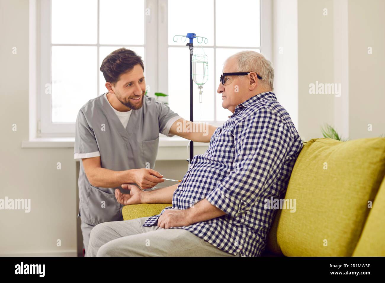 Young friendly nurse man helping a senior patient receiving iv drip ...