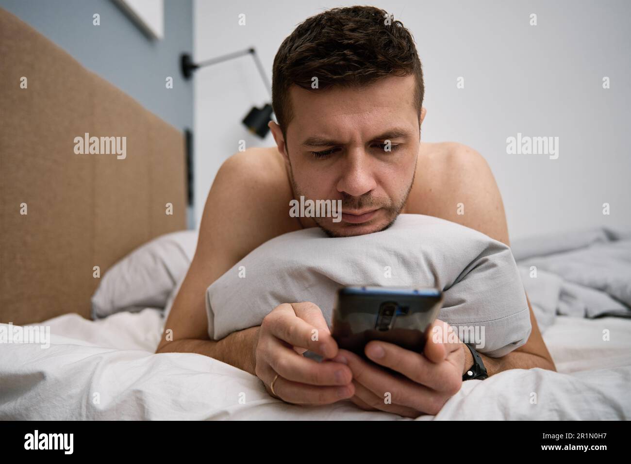 Phone addiction. Man lying in bed with smartphone. Man resting in ...