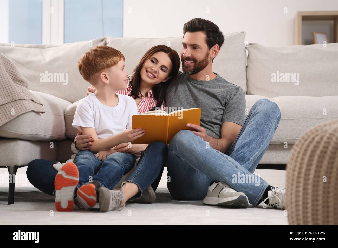 Happy parents with their child reading book on floor at home Stock ...