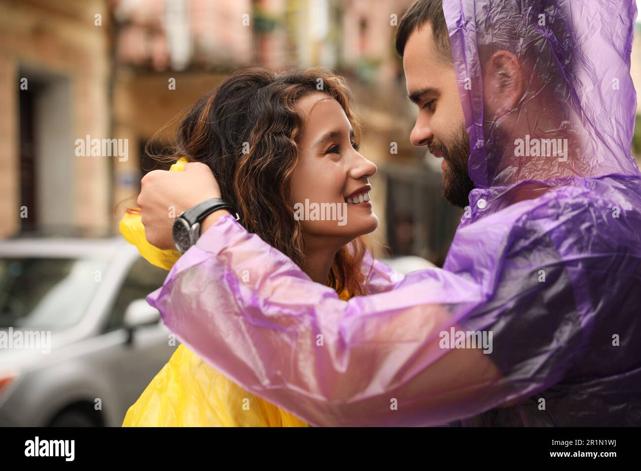 Young Couple In Raincoats Enjoying Time Together On City Street Stock