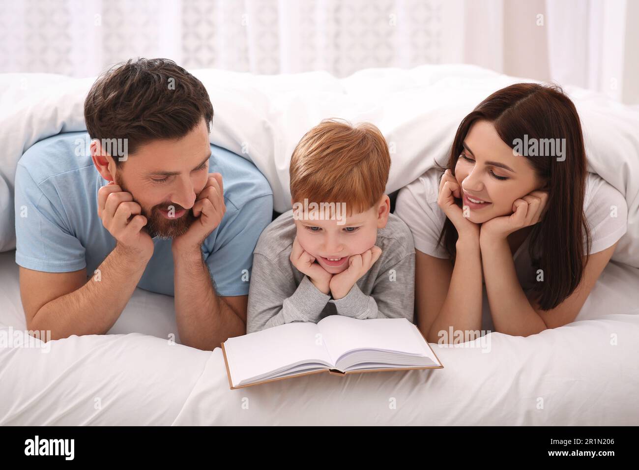 Happy parents with their child reading book on bed at home Stock Photo ...