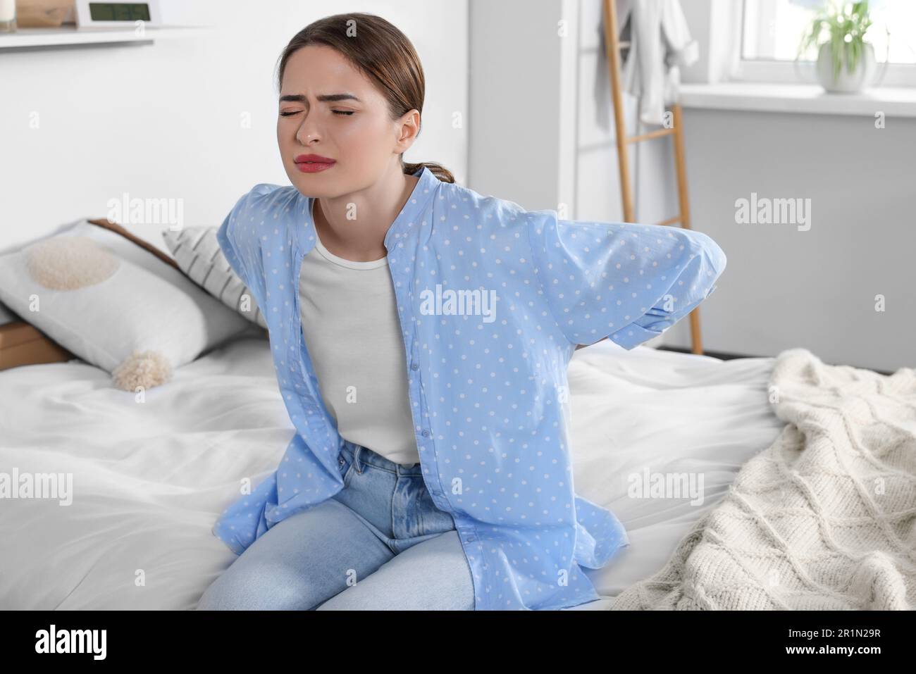 Woman suffering from back pain while sitting on bed at home. Symptom of ...