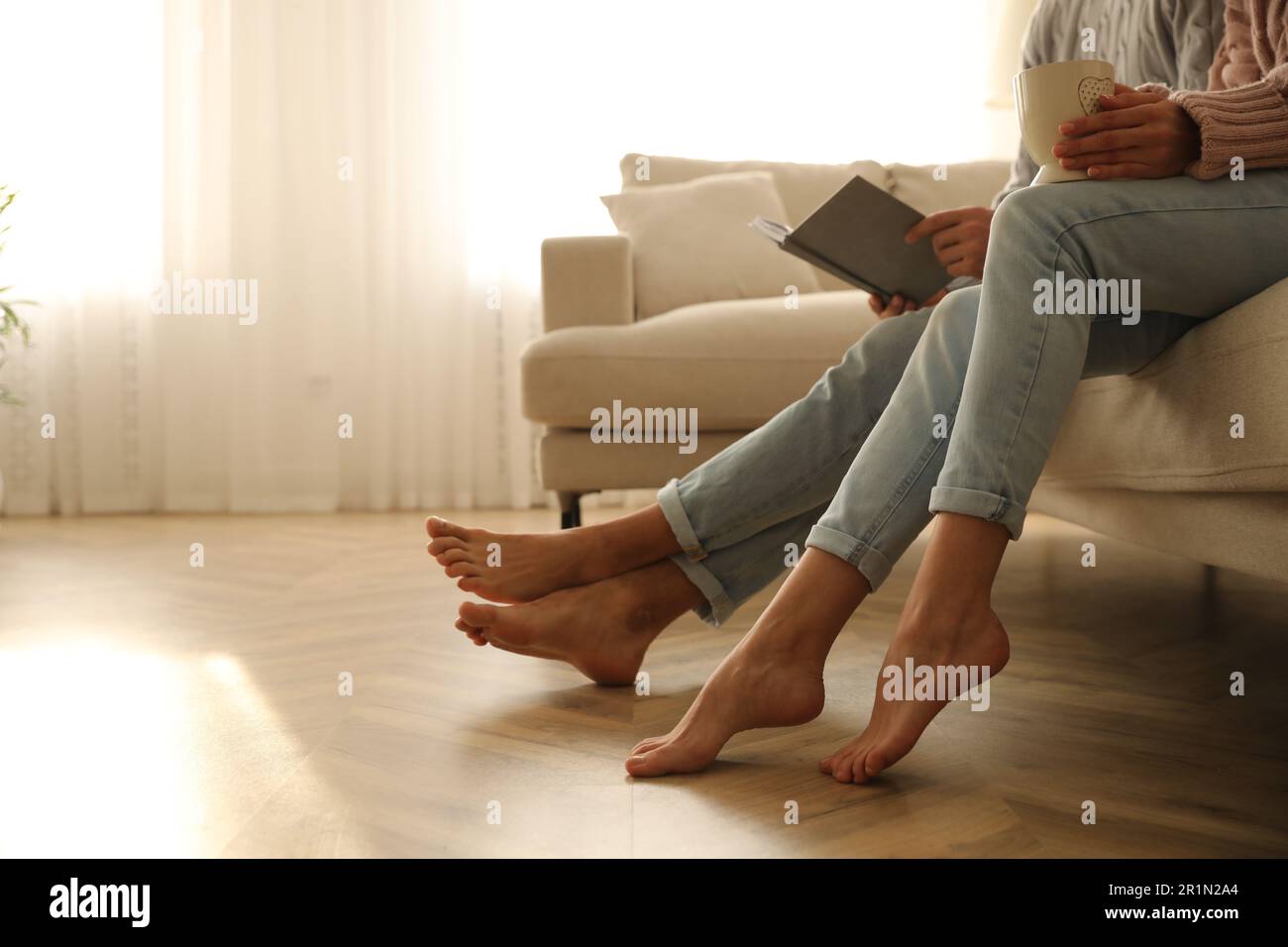 Barefoot couple sitting on sofa in living room, closeup. Floor heating ...