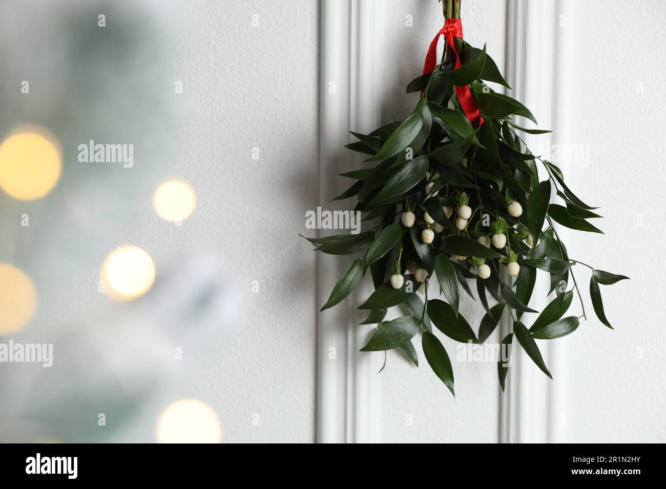 Mistletoe bunch with red ribbon hanging on light background, space for ...
