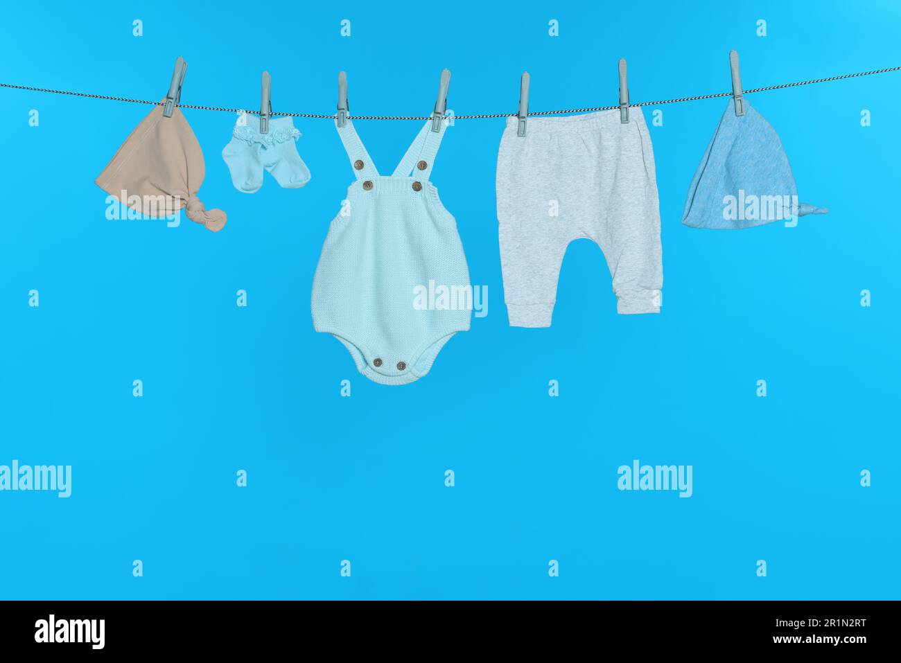Different baby clothes drying on laundry line against light blue ...