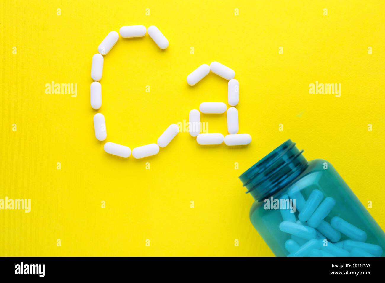 Open bottle and calcium symbol made of white pills on yellow background ...