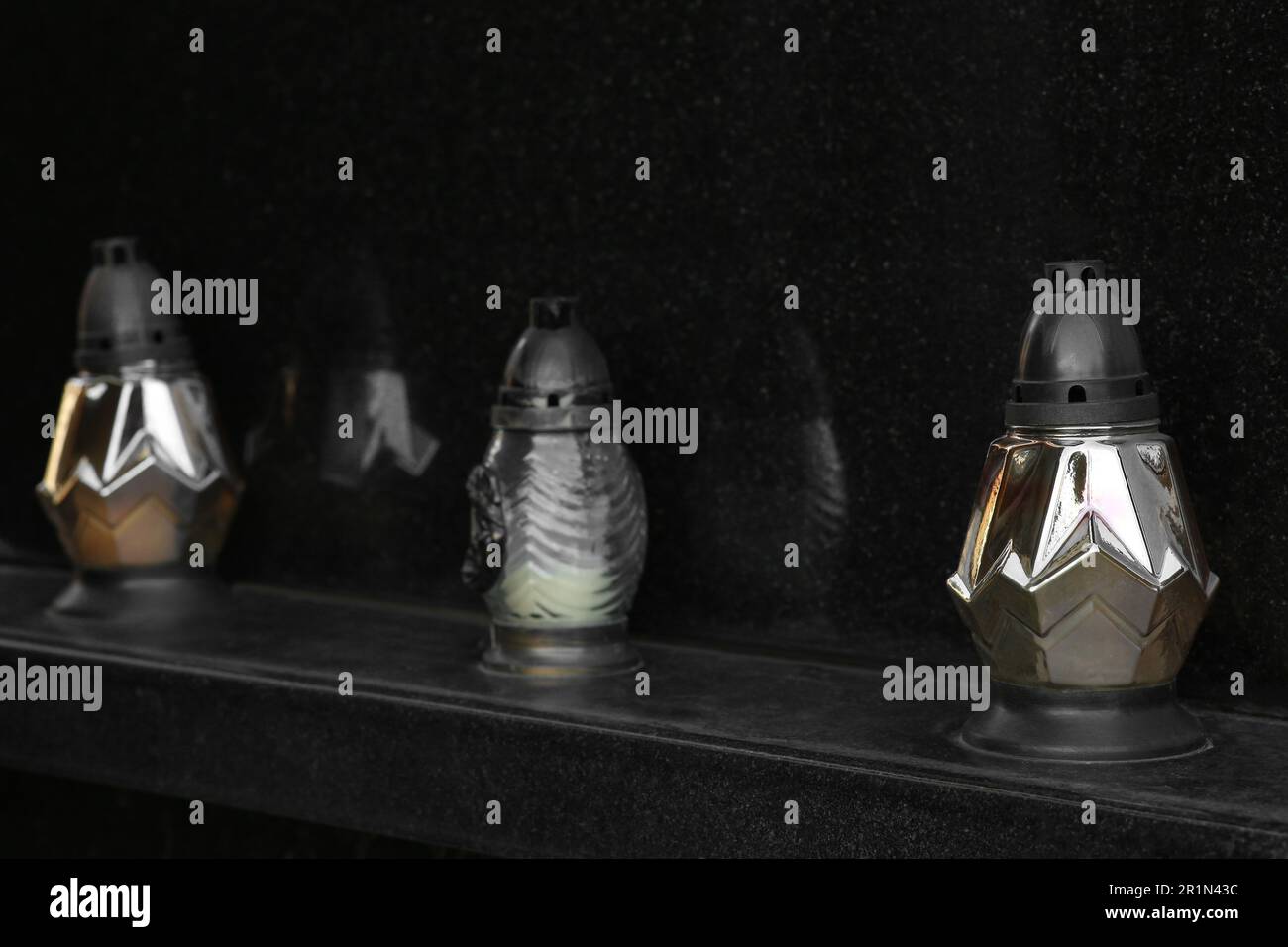Different grave lanterns on black tombstone. Funeral ceremony Stock Photo - Alamy