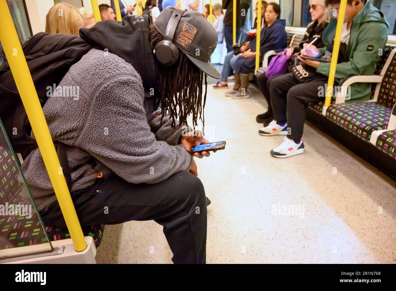 London, England, UK. Man with dreadlocks looking at his phone on a tube ...