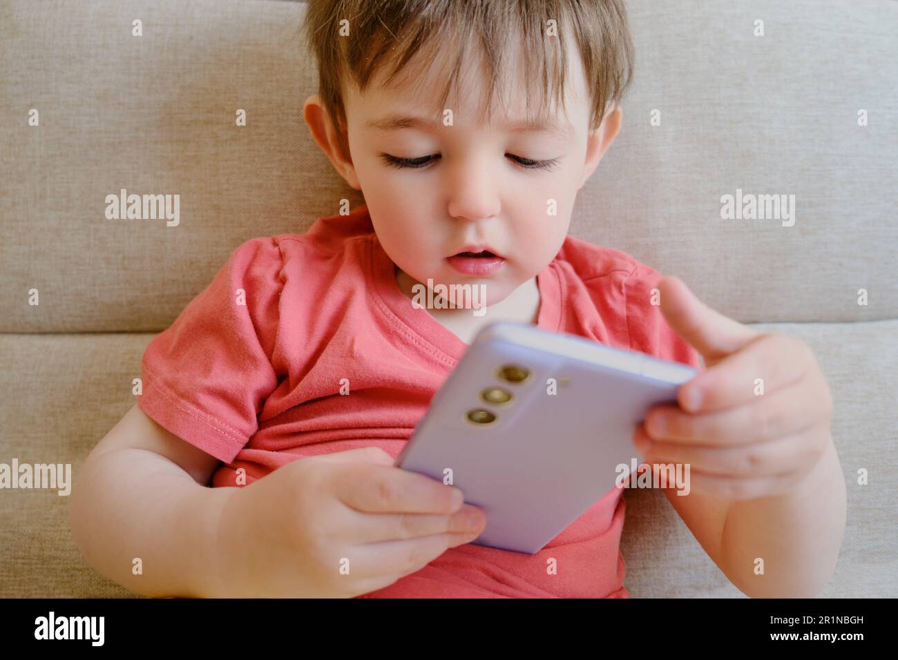 Baby is busy tapping the phone screen. The phone-holding child looks ...