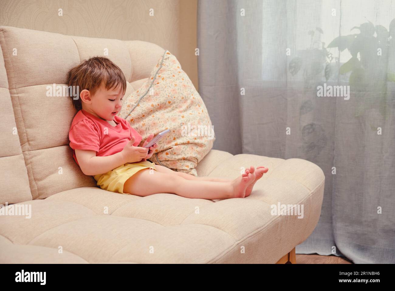 The little boy uses his finger to touch the screen of the mobile device ...