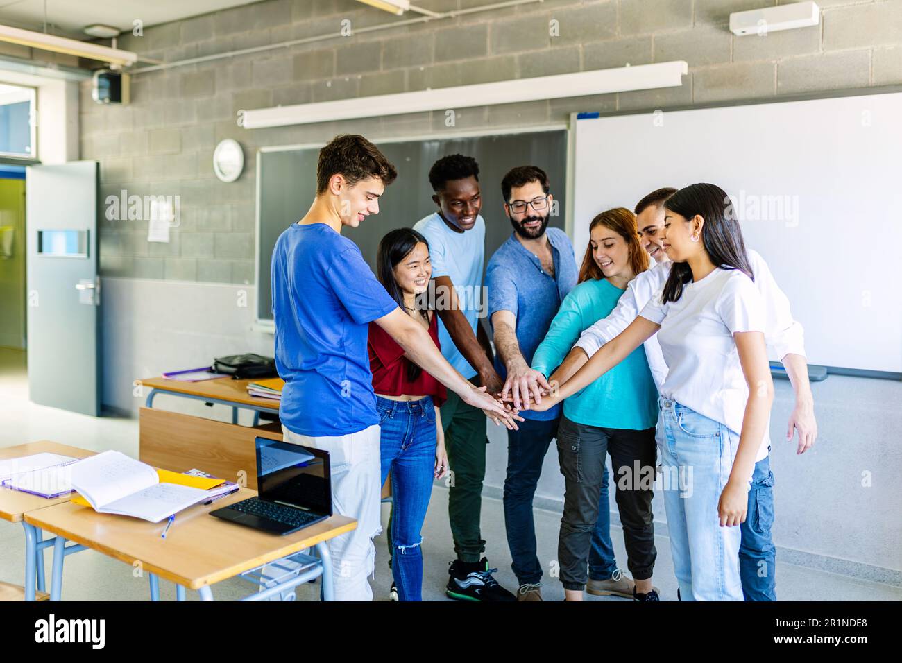 Young group of student classmates stacking hands with teacher in ...