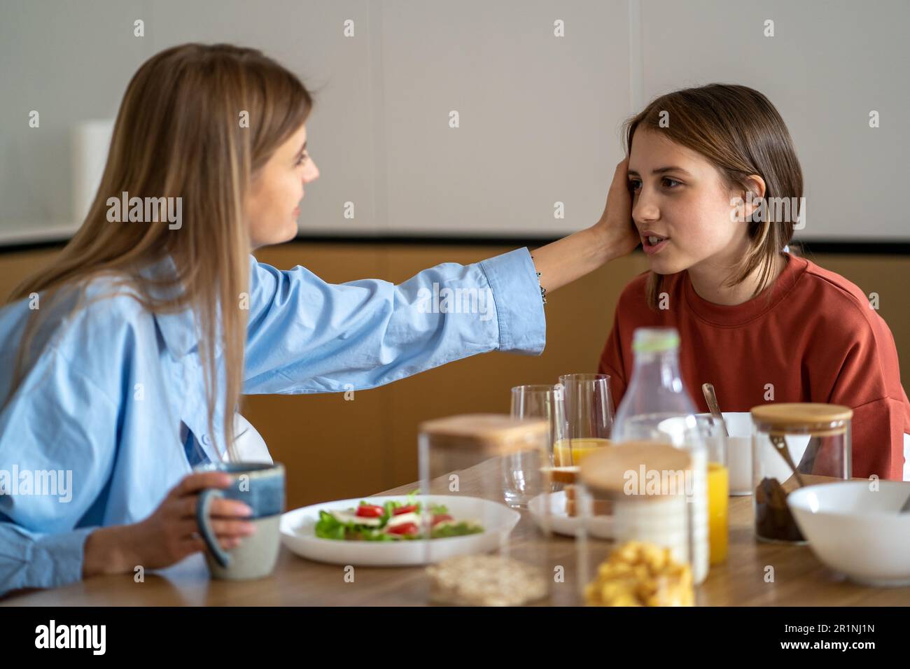 Caring mom gentle touch head teen girl sitting at table on morning ...