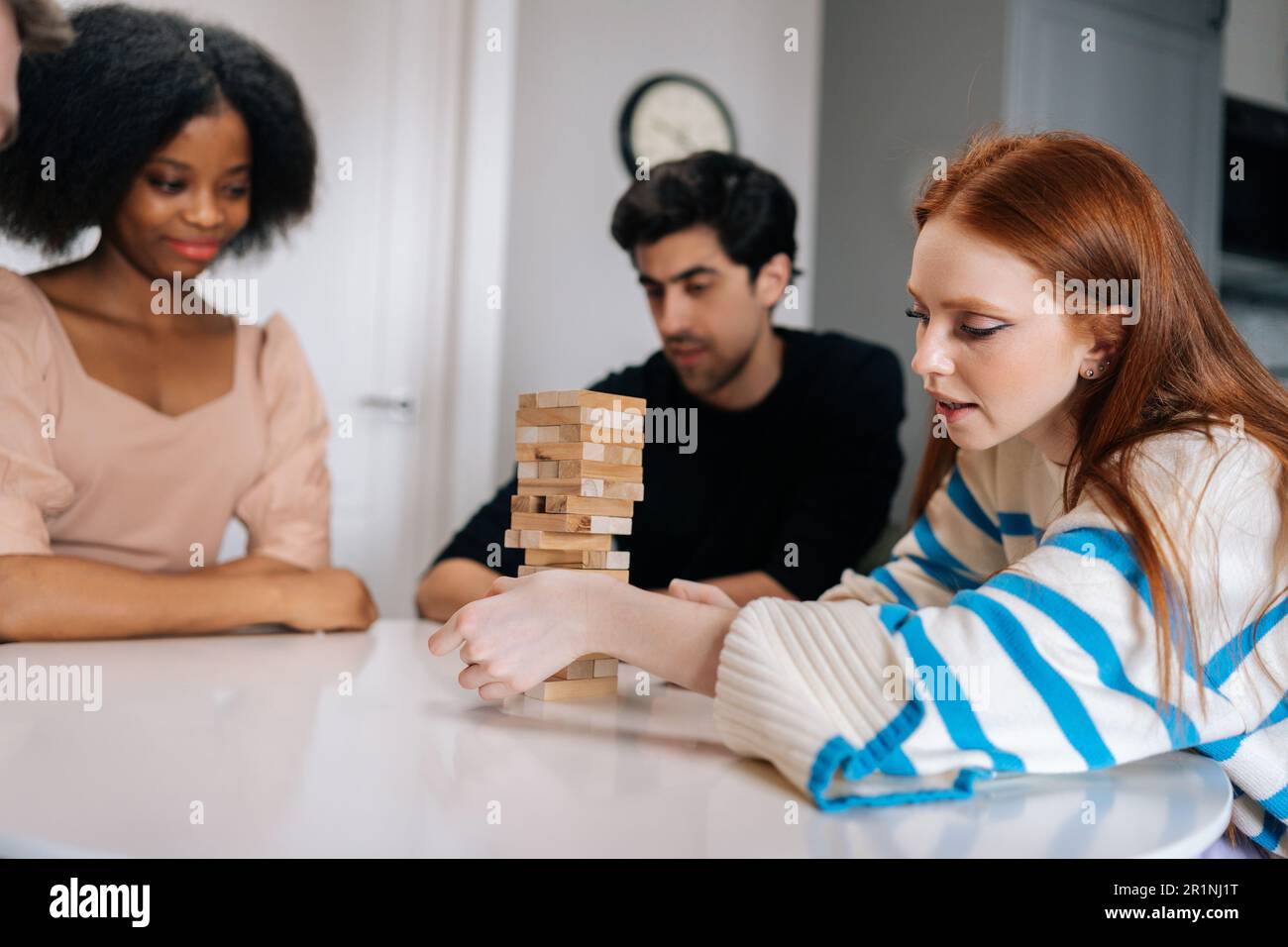 Side view of focused young redhead female carefully taking jenga wooden ...