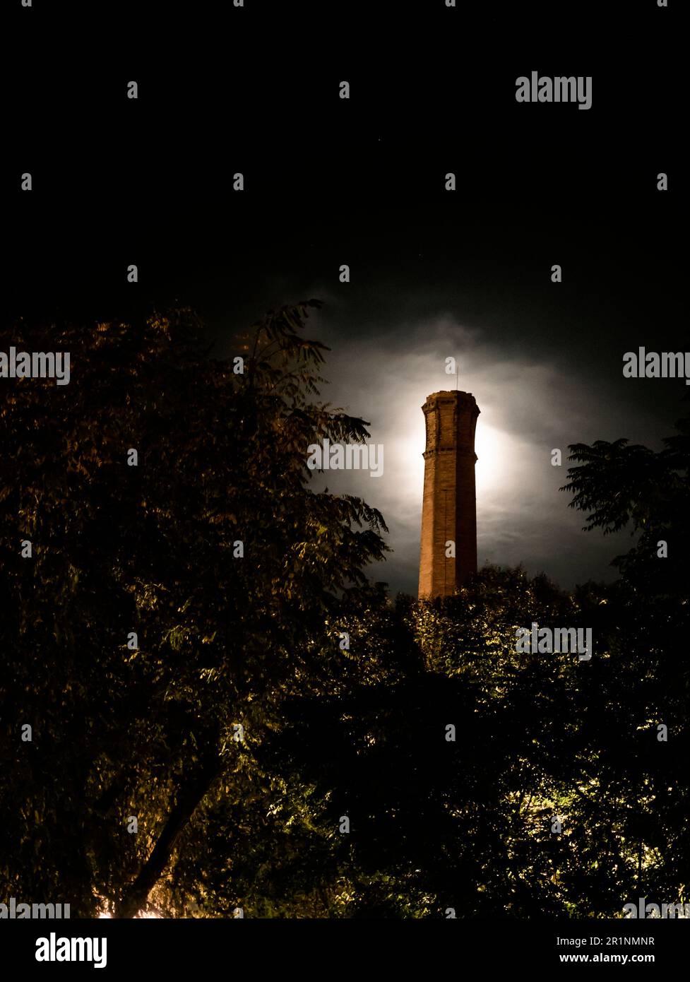 Chimney of old oil mill illuminated by the full moon between the mist ...