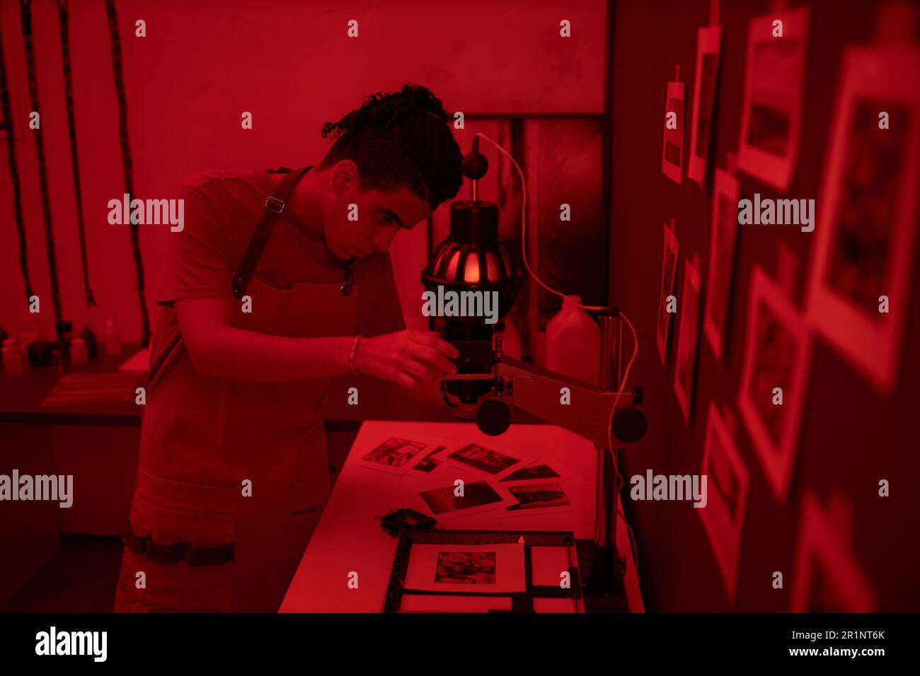 Young photographer using special equipment to make photo in darkroom ...