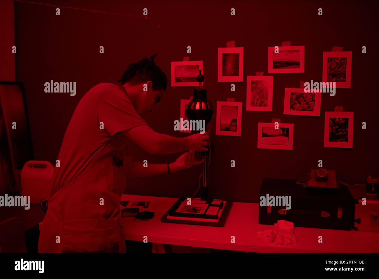Young photographer working with special equipment in darkroom with red ...